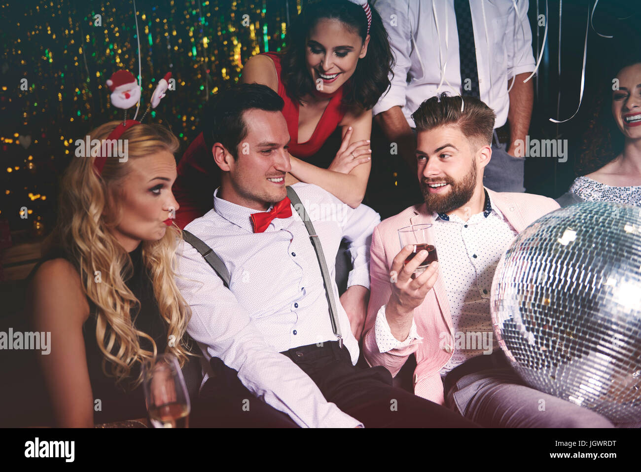 Group of friends sitting together at party, man holding disco ball in ...