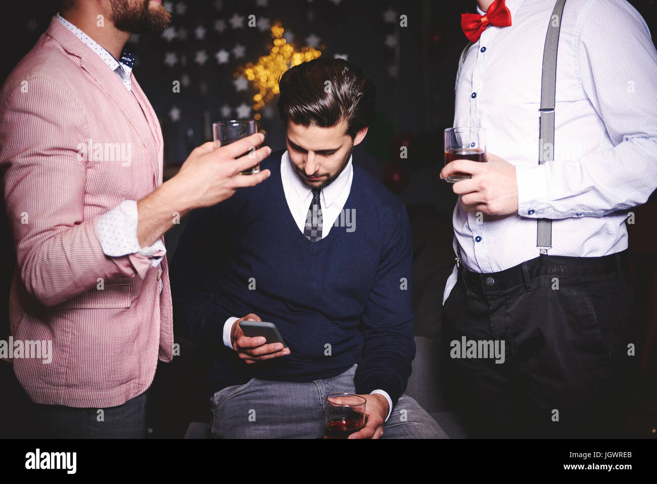 Three men at party, man in middle using smartphone Stock Photo - Alamy