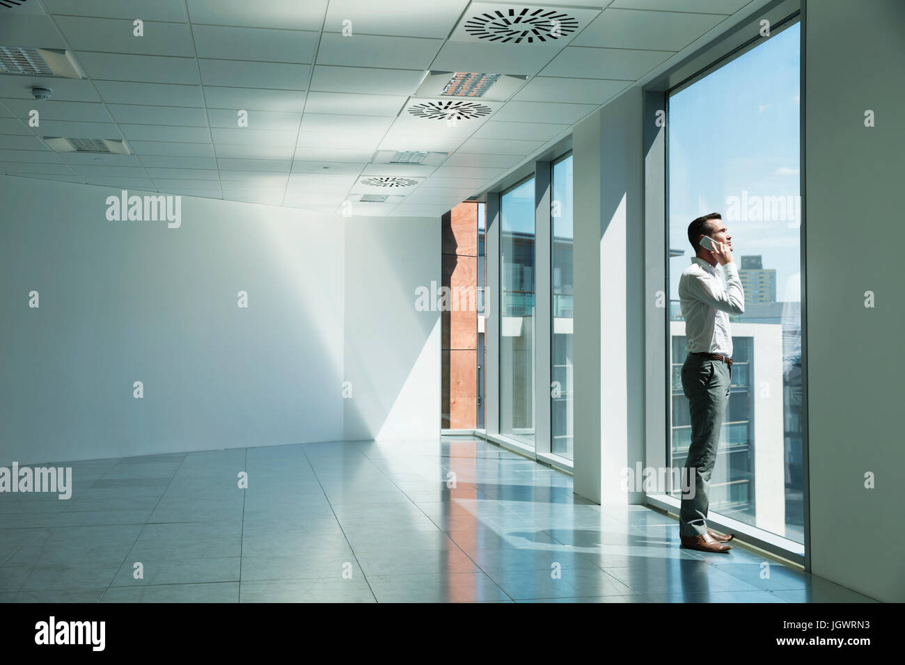 Businessman, looking out of window in empty office space, using ...
