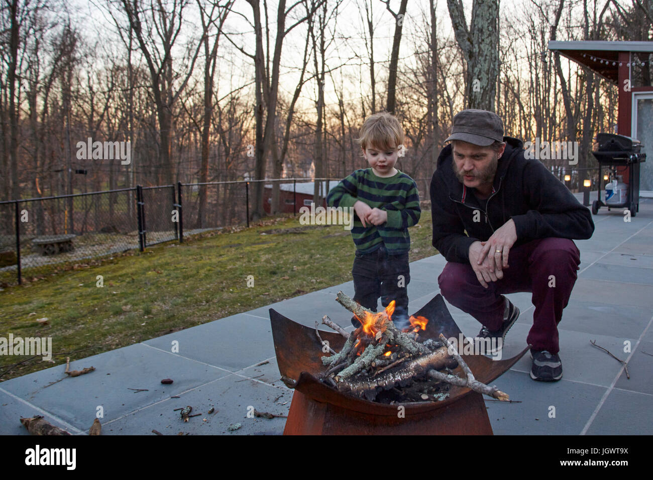 Boy and father tending fire in patio fire pit Stock Photo - Alamy