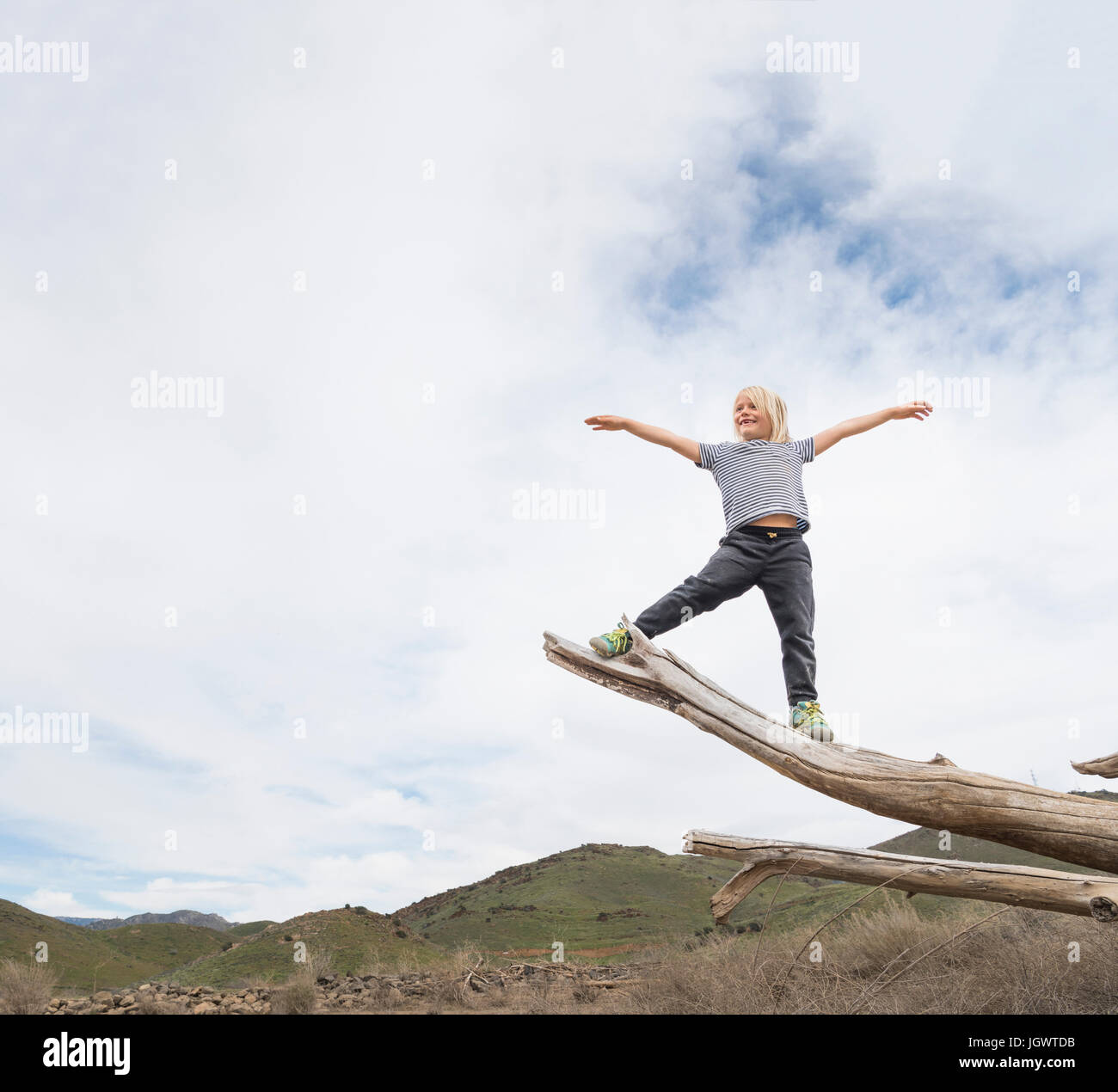 Boy balancing on end of tree trunk, sky in background Stock Photo - Alamy