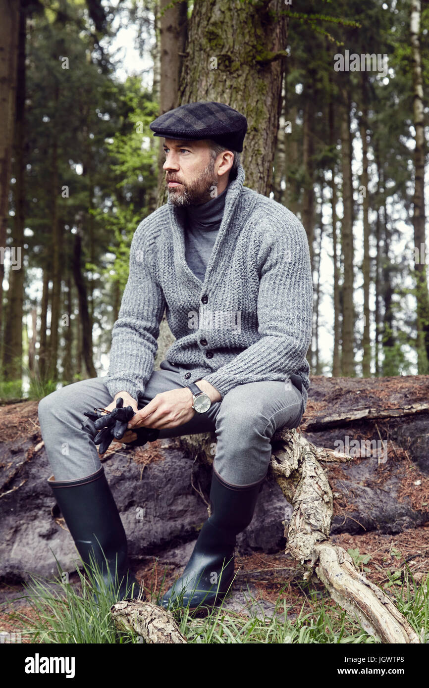 Man in outdoor clothes looking out from woodland log Stock Photo - Alamy