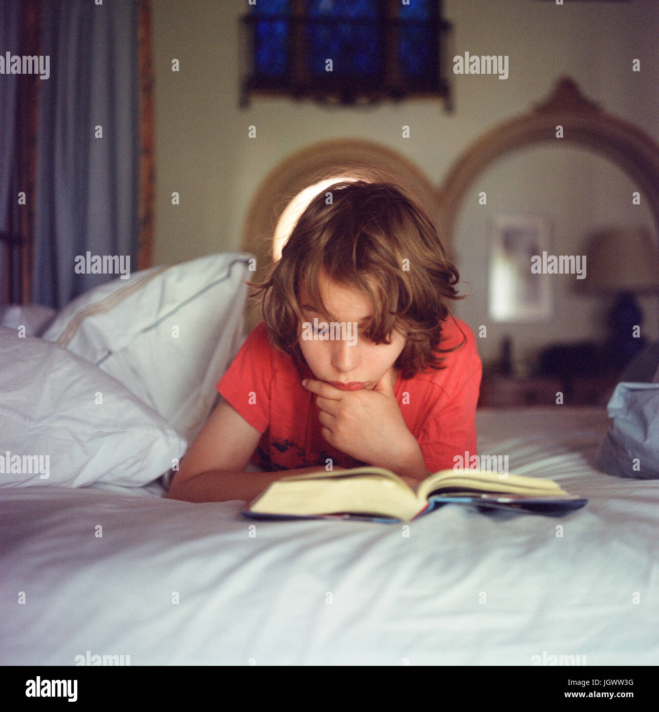 Boy relaxing on bed, reading book Stock Photo - Alamy
