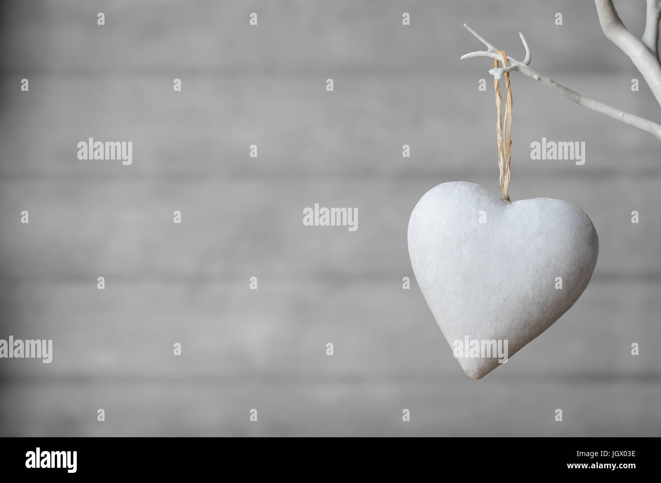 A white painted heart, hanging from branch of white artificial tree ...