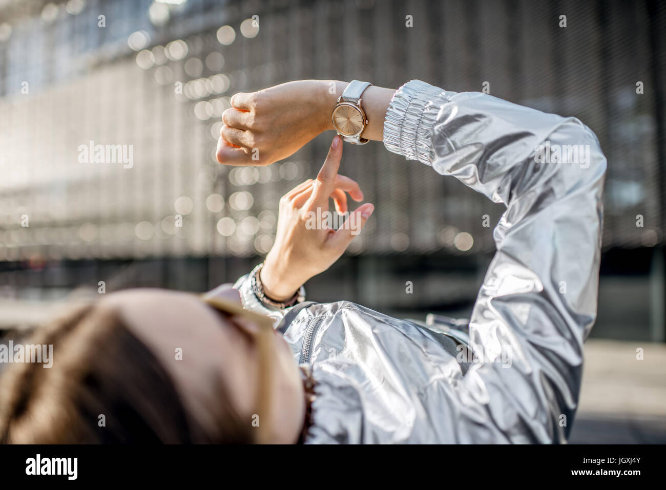 Stylish woman in silver jacket watching the clock lying outdoors at the ...