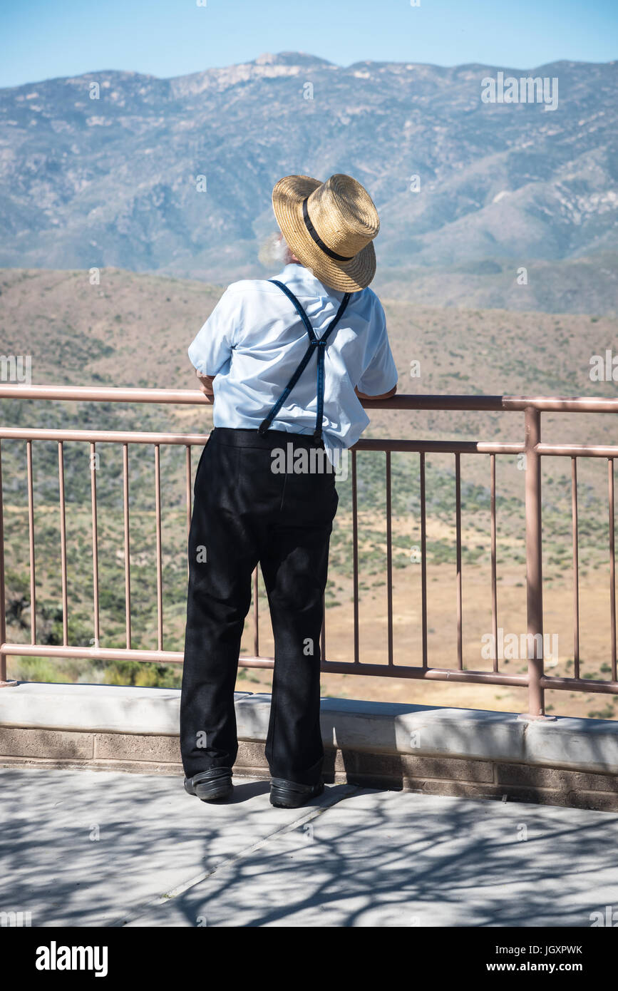 Amish man in a straw hat on a viewing platform observes a mountain ...