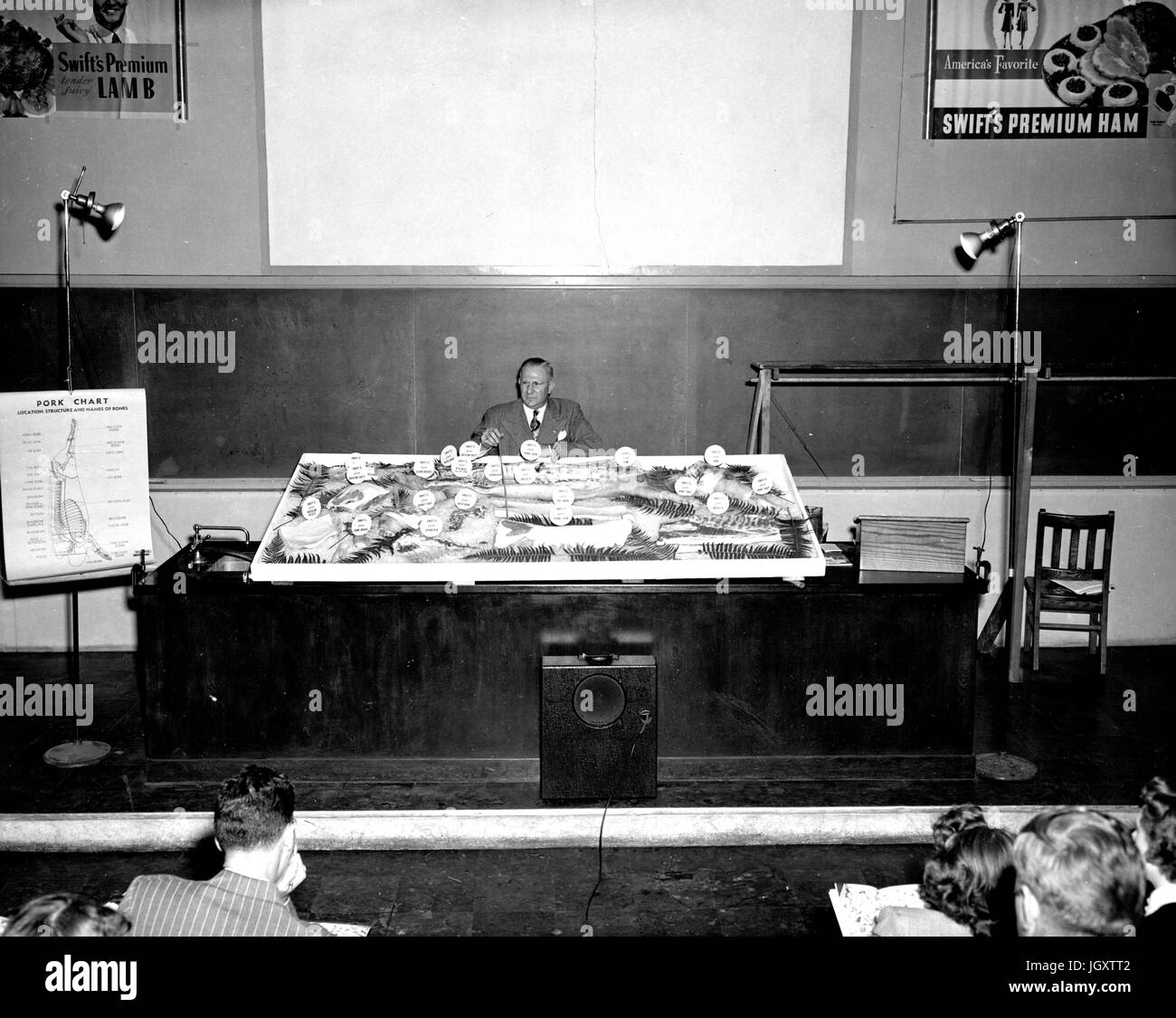 A professor stands at the front of a lecture hall addressing the class ...