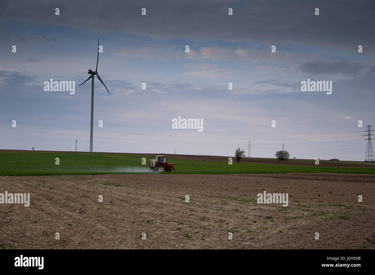 landscape with wind turbine and old tractor spraying pesticides on ...