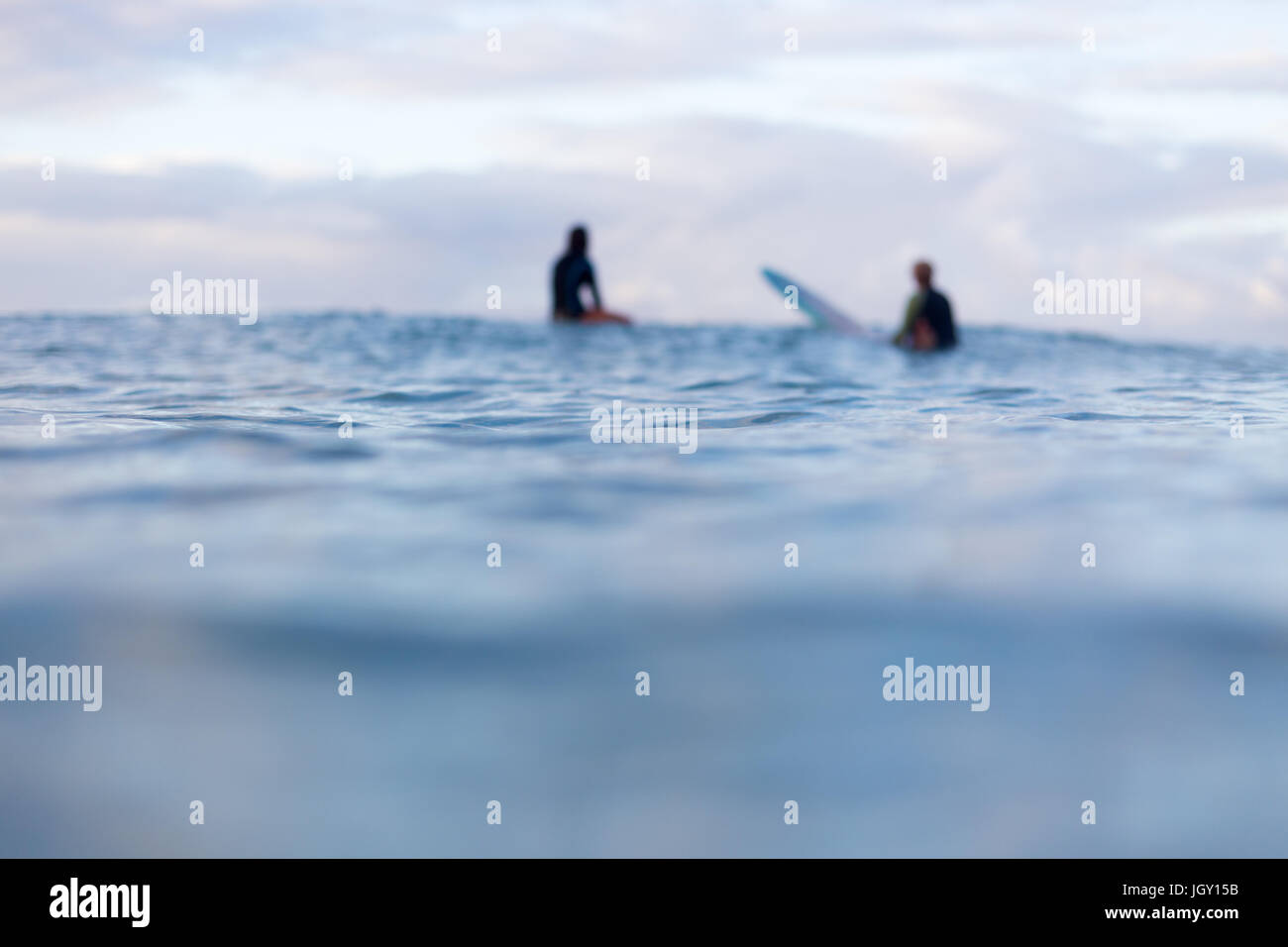 Two out of focus surfers sit in the distance on their surfboards as ...