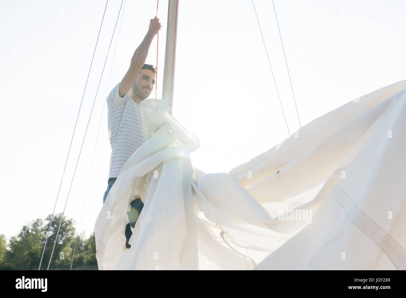 Man on sailing boat, taking down sail Stock Photo - Alamy