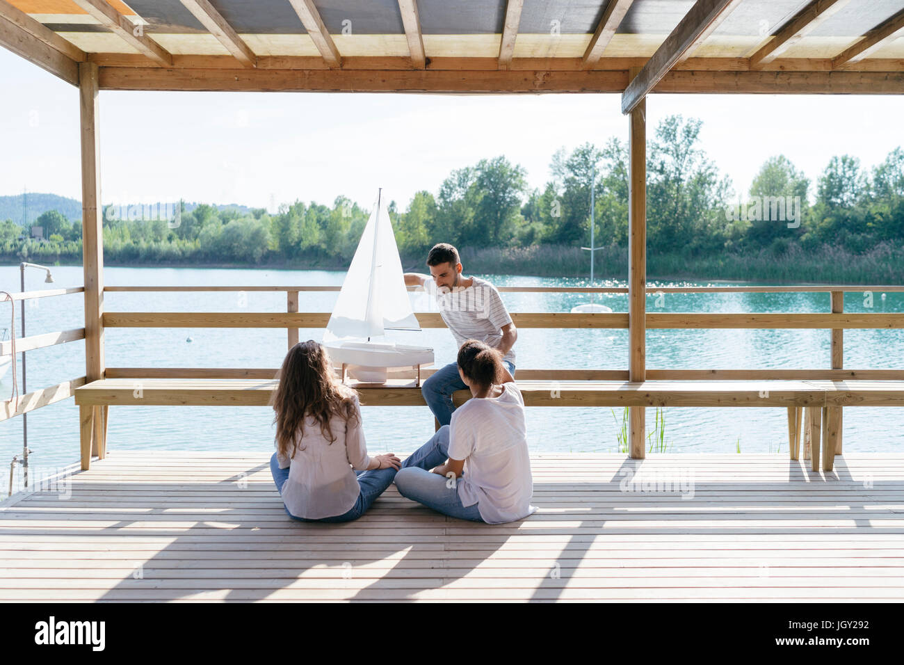 Three friends at nautical club, sitting on pier talking, model sailing ...