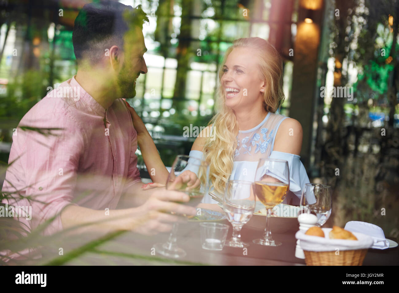 Window view of young woman with boyfriend laughing at restaurant table ...