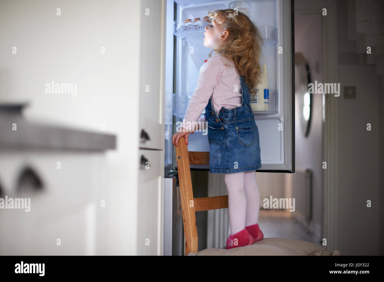 Young girl standing on chair, looking into fridge Stock Photo - Alamy