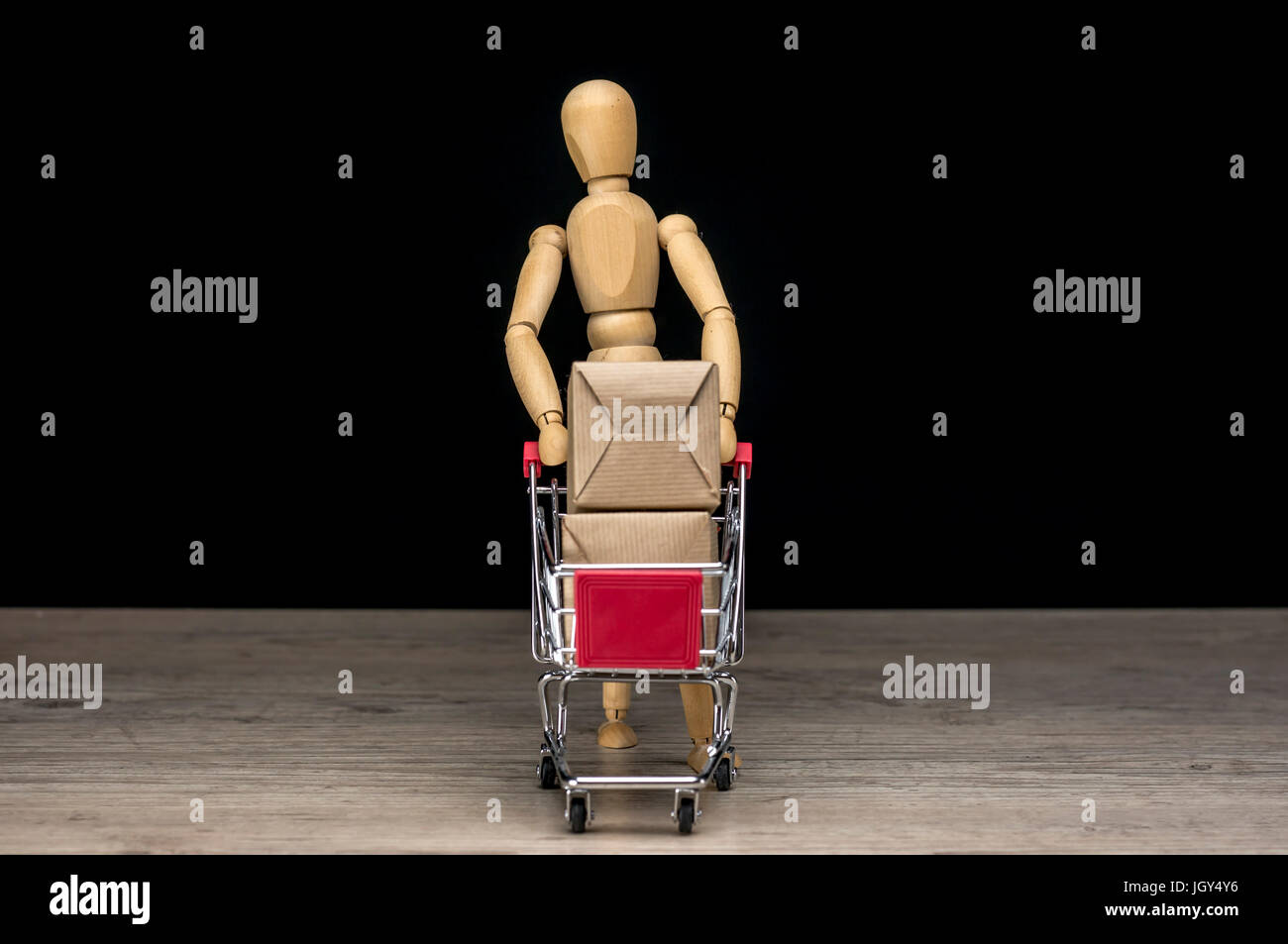 Wooden human mannequin holding shopping trolley filled with parcels ...