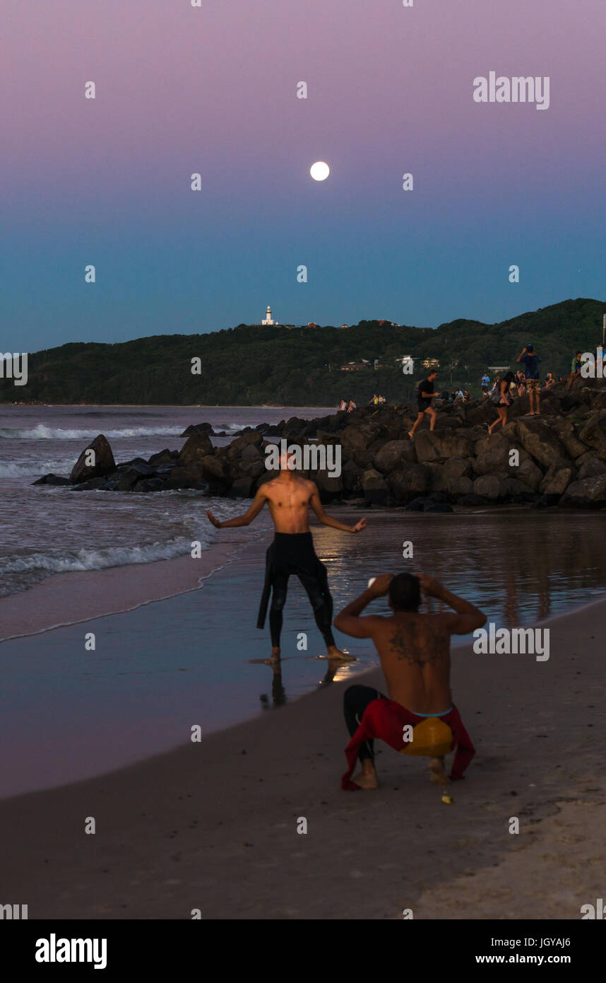 People watch the sun set and full moon rise at Byron bay, New South ...