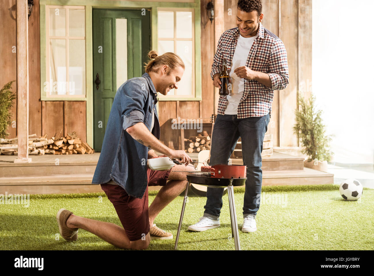 two men grilling burgers while talking and drinking beer outdoors Stock ...