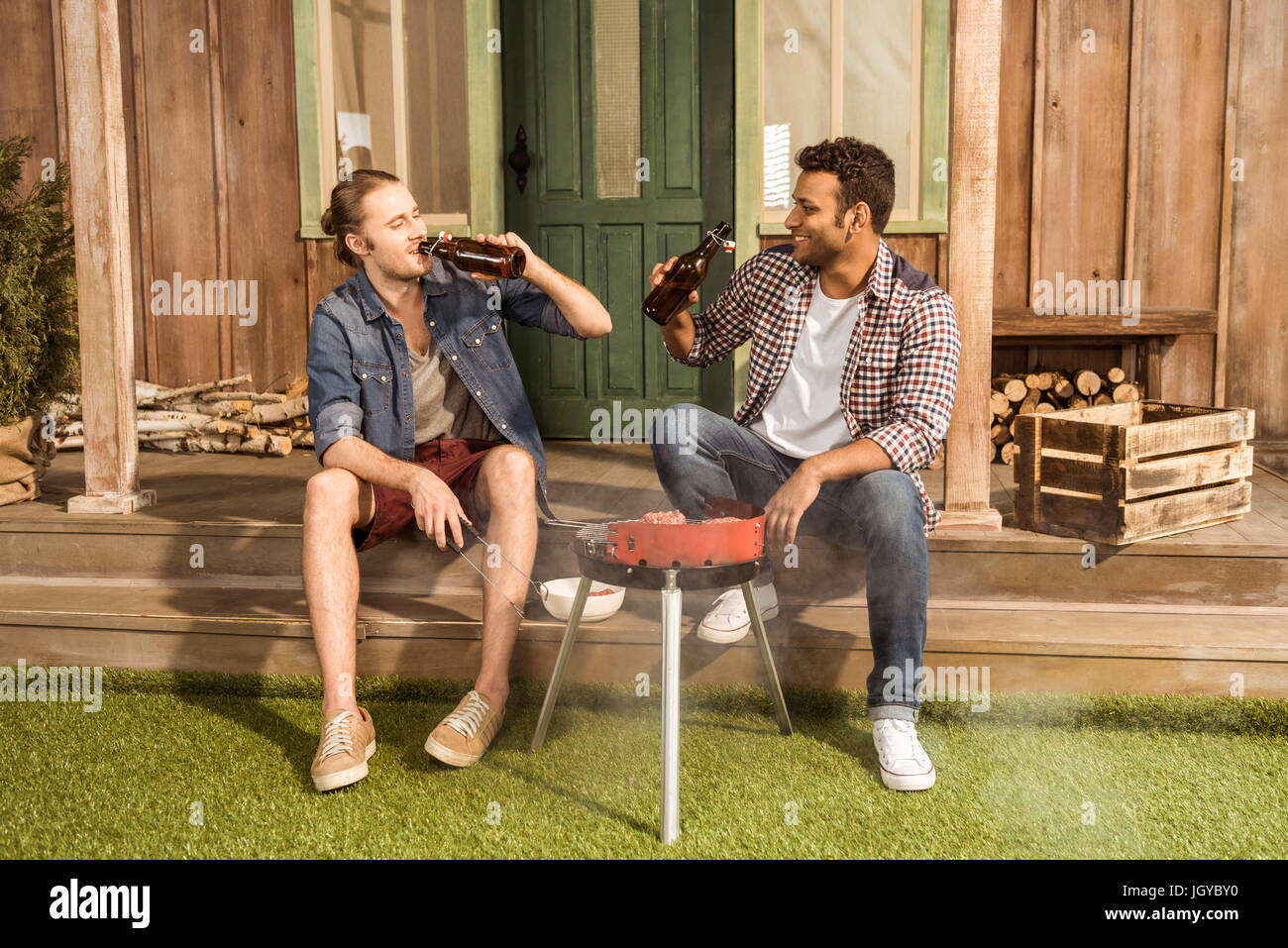 Two young men drinking beer and preparing meat on outdoor grill Stock ...