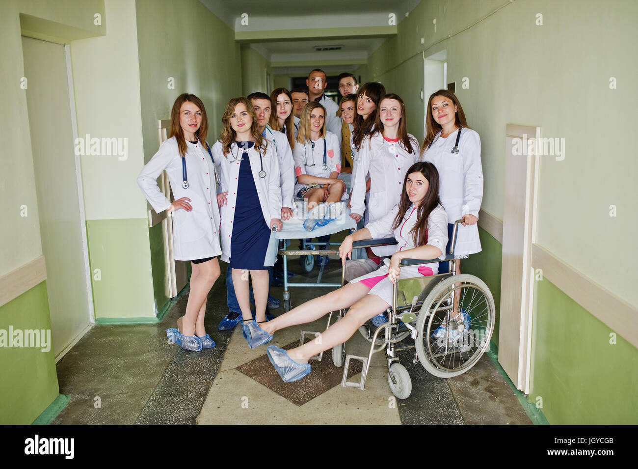 Crazy young doctors having fun by posing on a wheelchair in the hallway ...