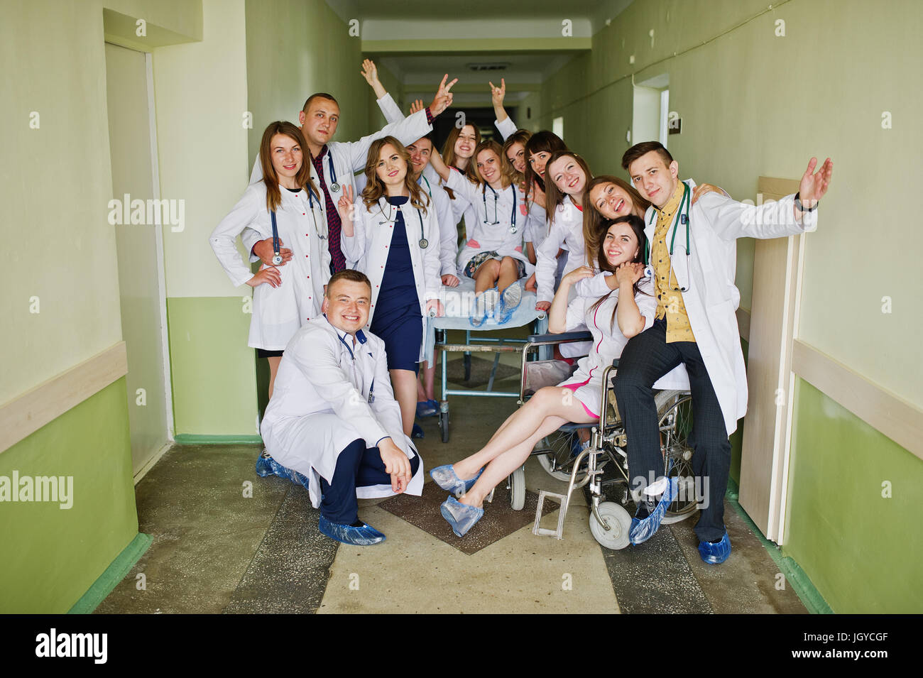Crazy young doctors having fun by posing on a wheelchair in the hallway ...