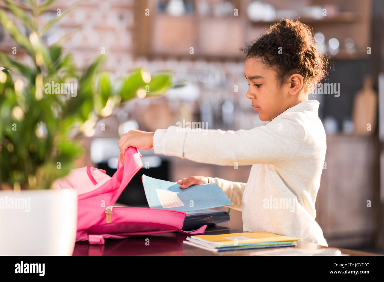 african american schoolgirl packing backpack and preparing for school ...