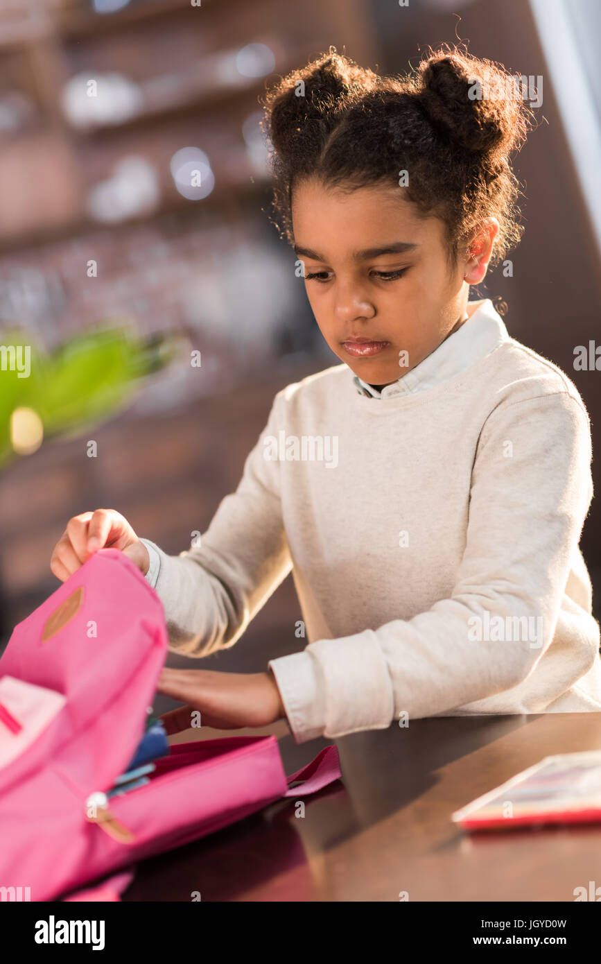 african american schoolgirl packing backpack and preparing for school ...