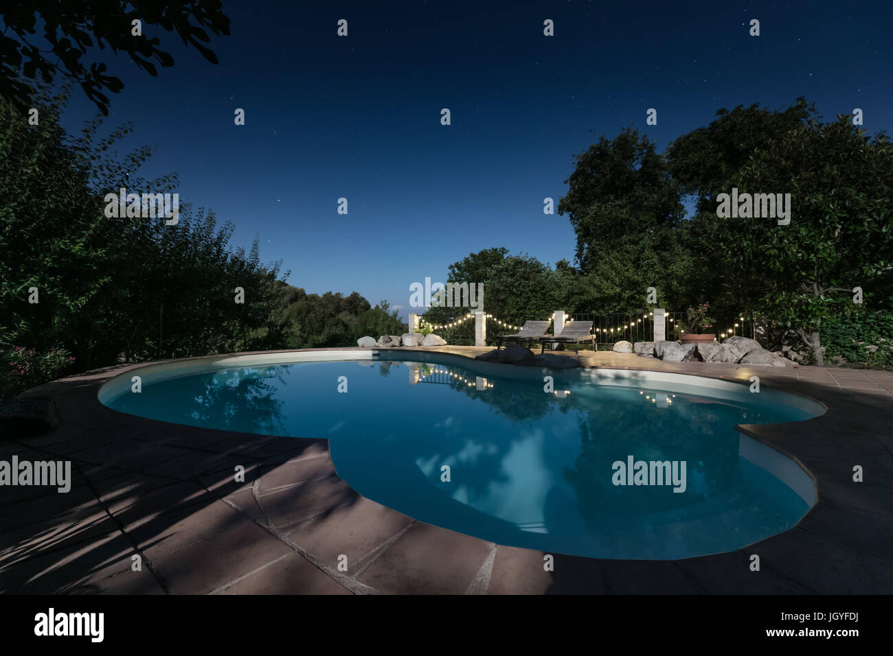 Moonlight lighting up a swimming pool on a clear deep blue starry night ...