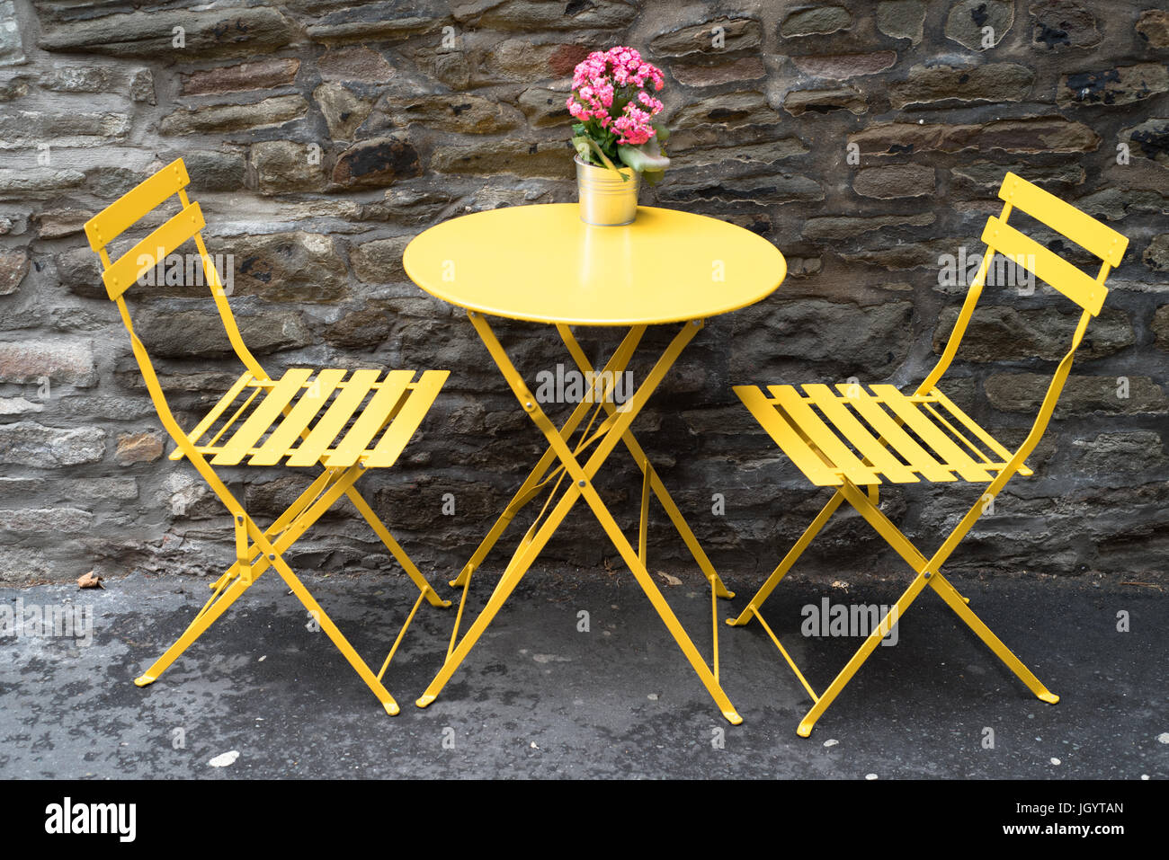 Empty bright yellow cafe tables and chairs against an interesting brick ...