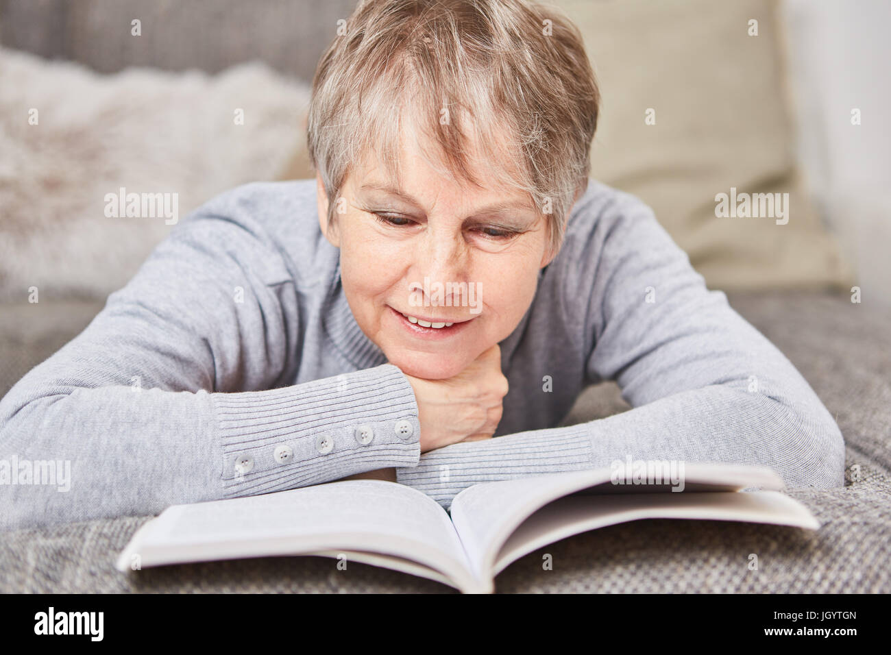 Senior woman with a book reading on the couch with excitement Stock ...
