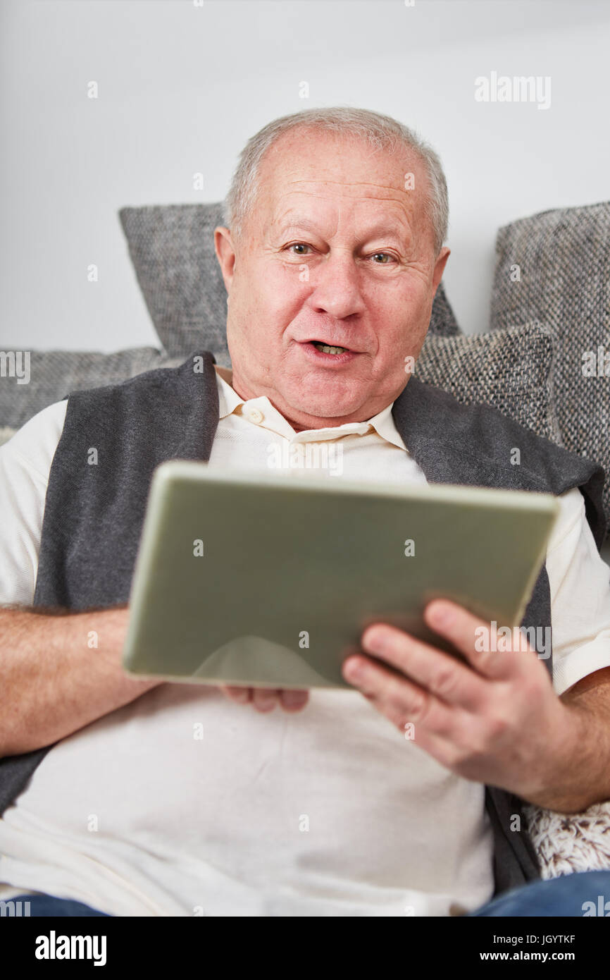 Senior man holding tablet computer at home on the couch Stock Photo - Alamy