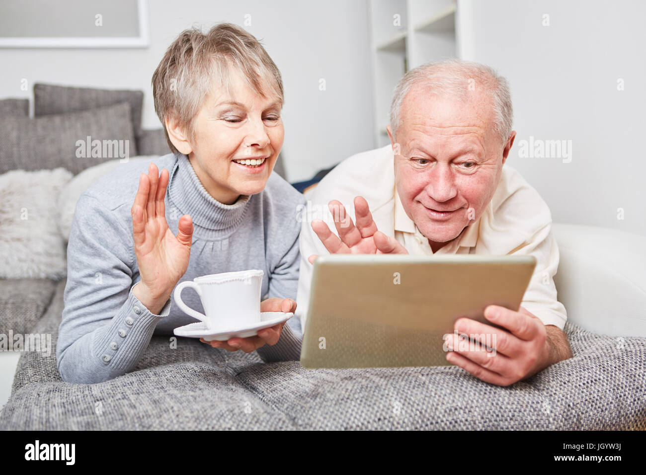 Seniors video chatting with tablet on the living room couch Stock Photo ...