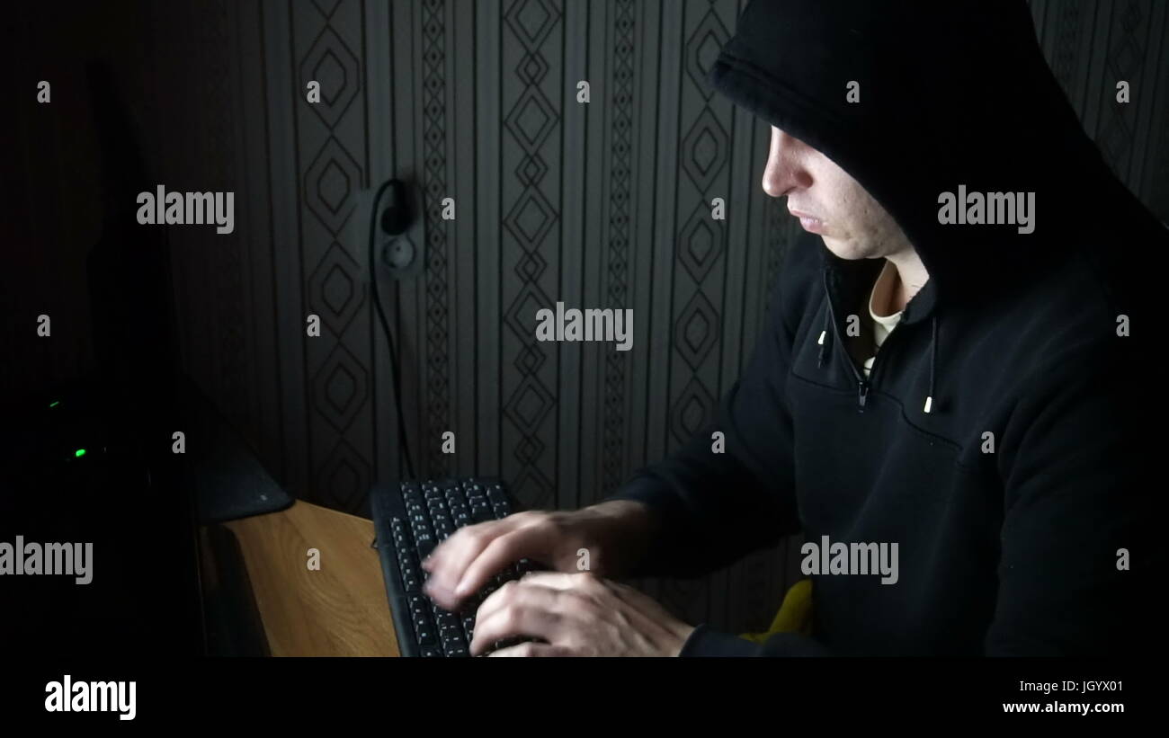Male hacker working on a computer in a dark office room Stock Photo - Alamy