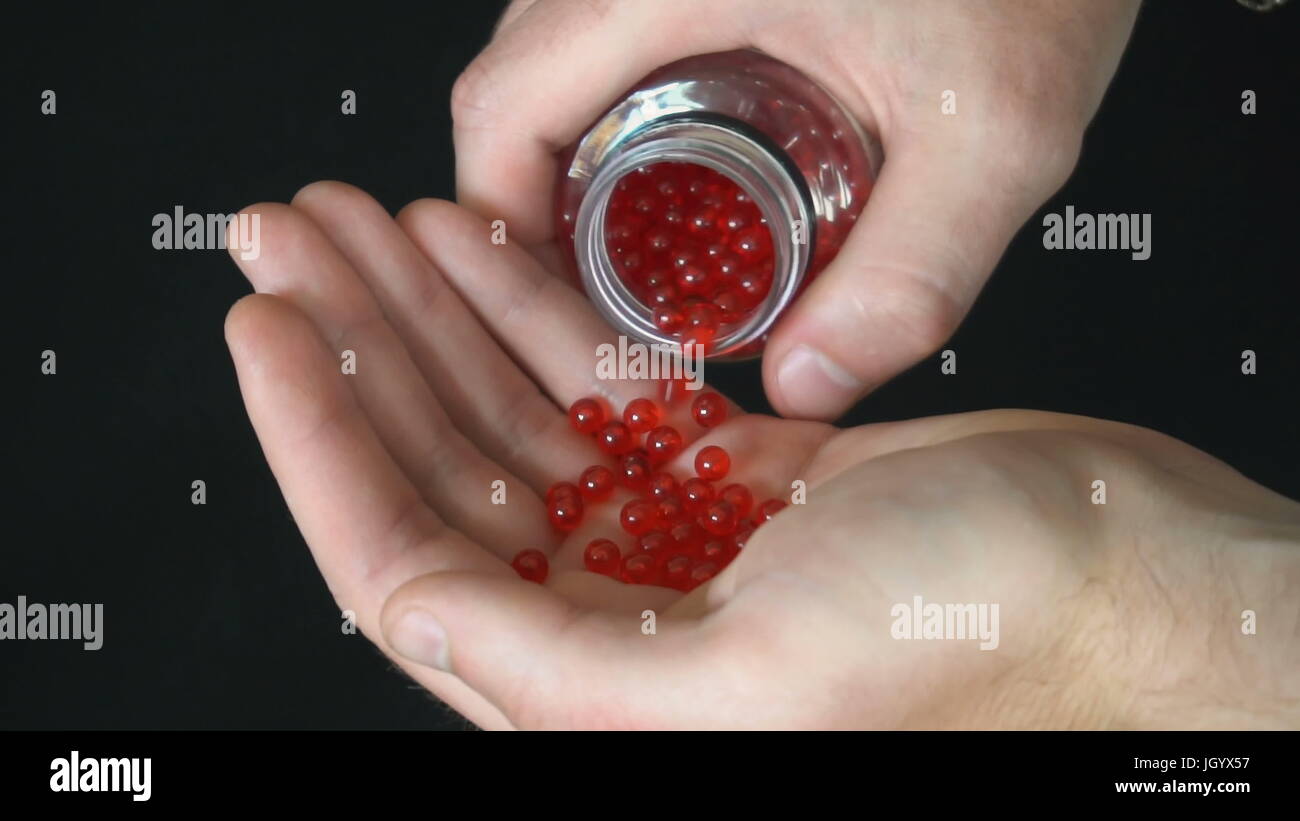 a young man pours it on the palm of his little red round pellets for ...