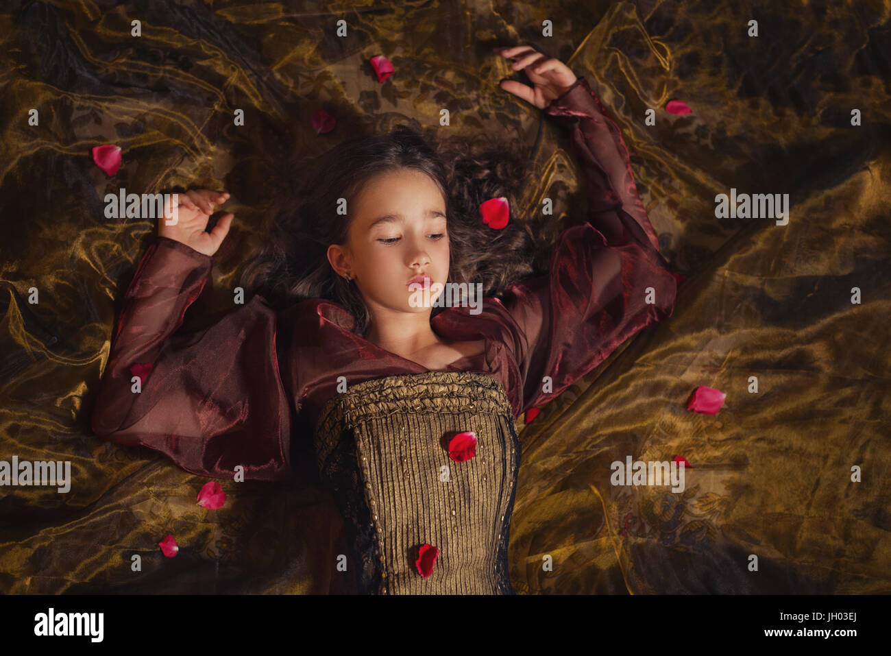 Portrait of cute young queen or princess laying on the ground covered ...