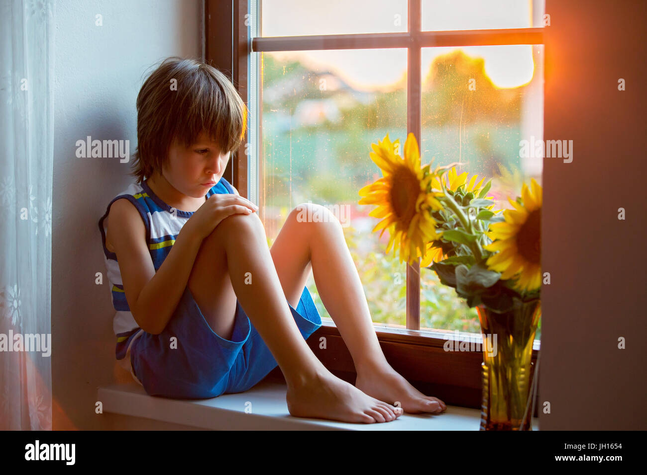 Sad cute little toddler child, sitting on a window, playing with ...