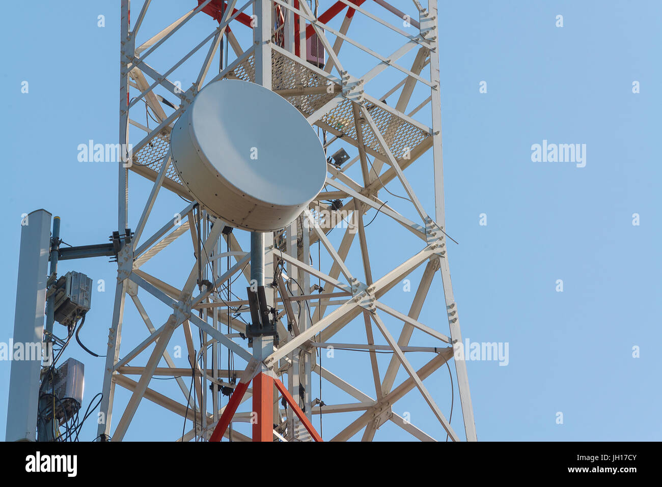 Mobile phone communication antenna tower with satellite dish on blue sky background ...