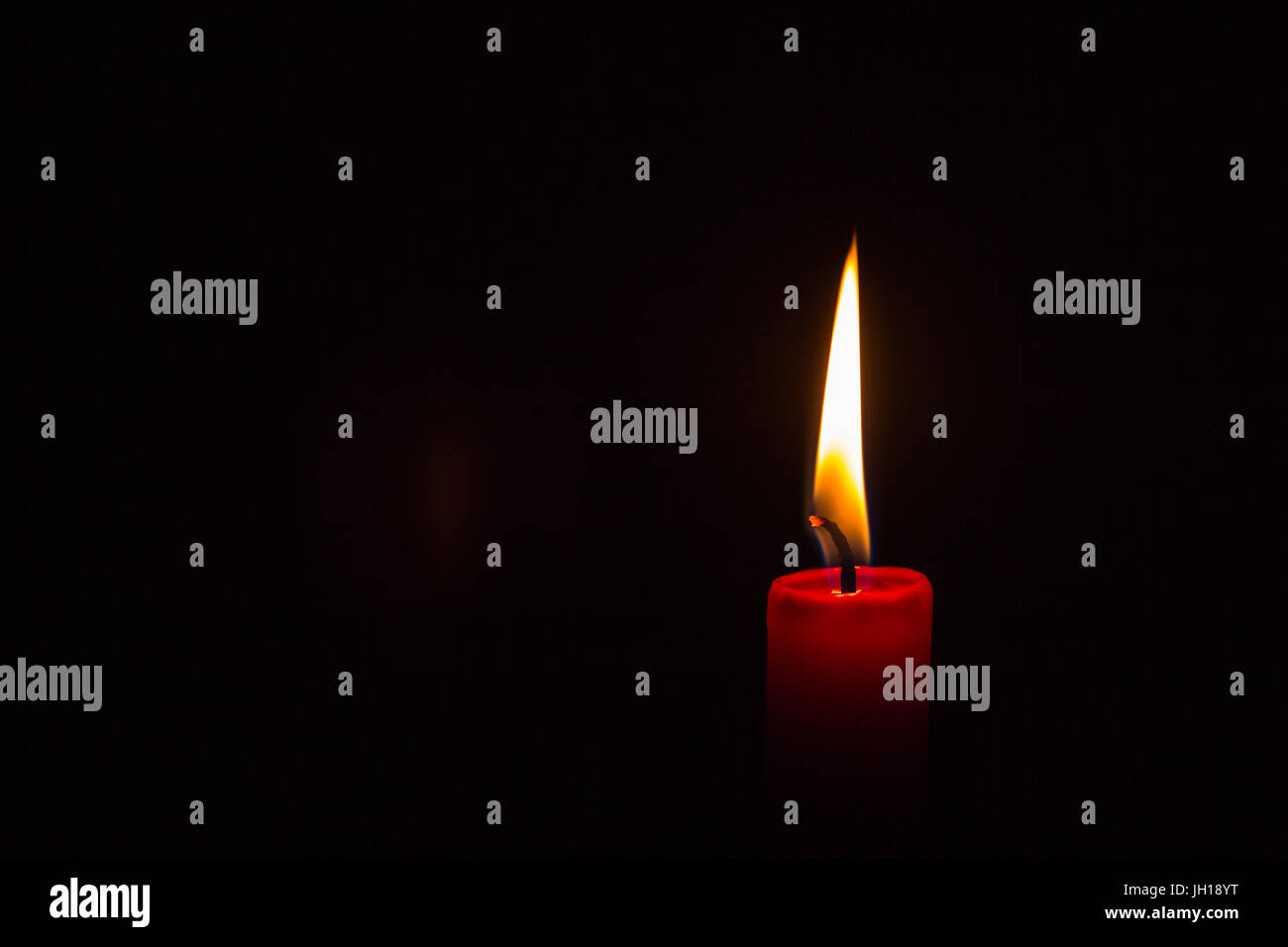 One small lit red candle on a black background Stock Photo - Alamy