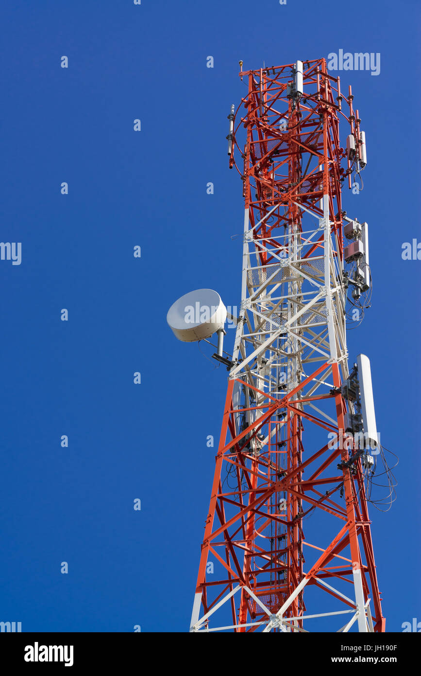 Mobile phone communication antenna tower with satellite dish on blue sky background ...