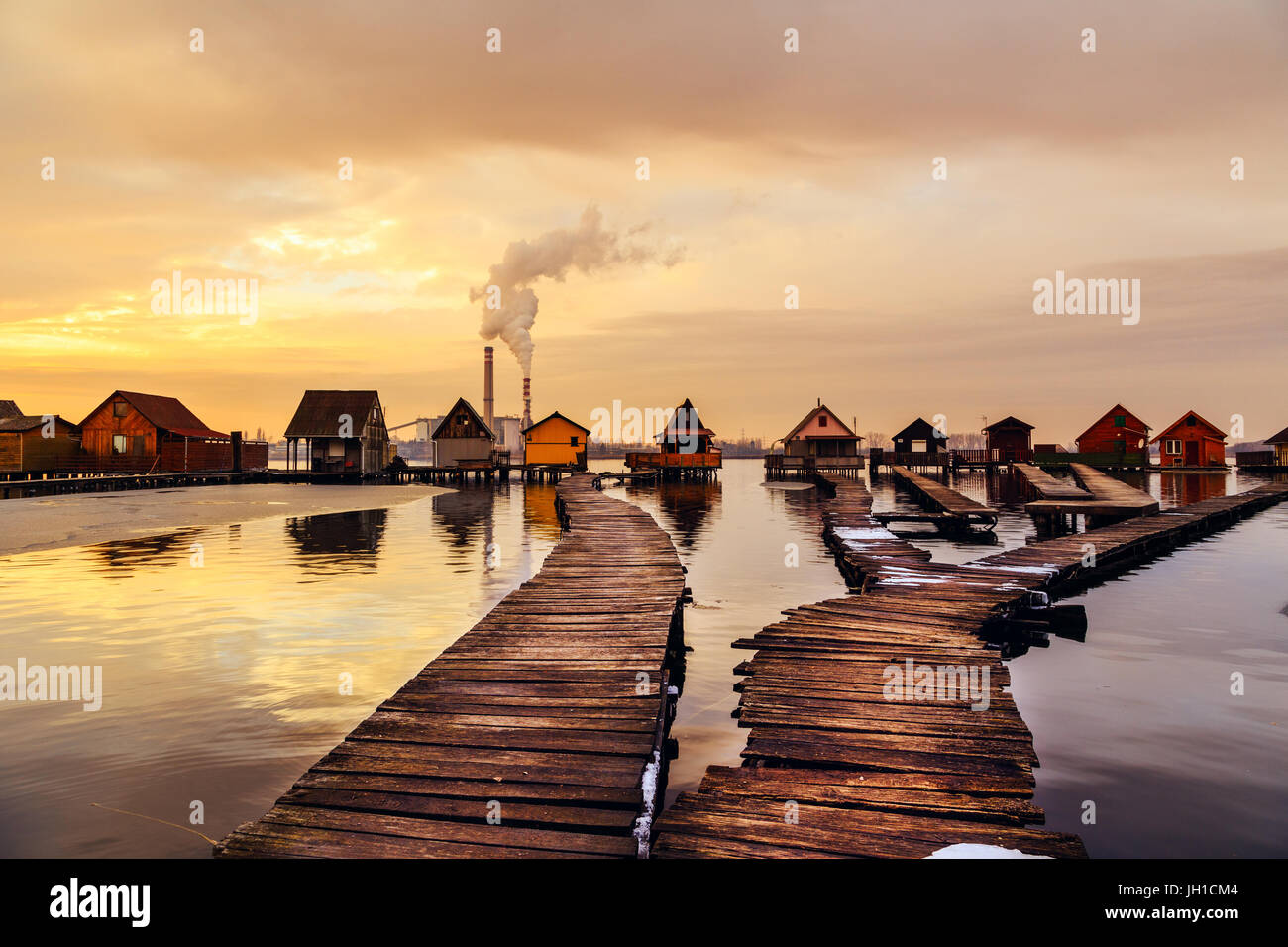 Sunset lake Bokod with pier and fishing wooden cottages, power plant in ...
