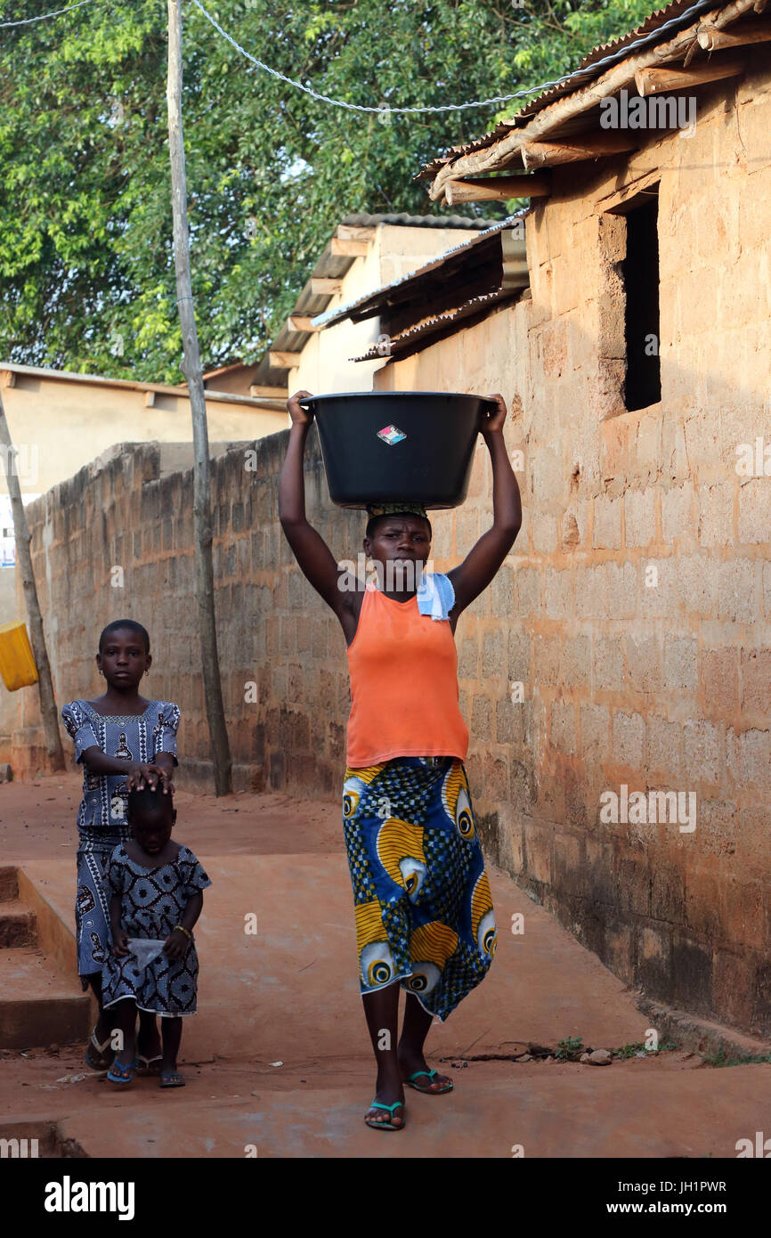 African village life. Water chore. African girl carrying a basin of ...