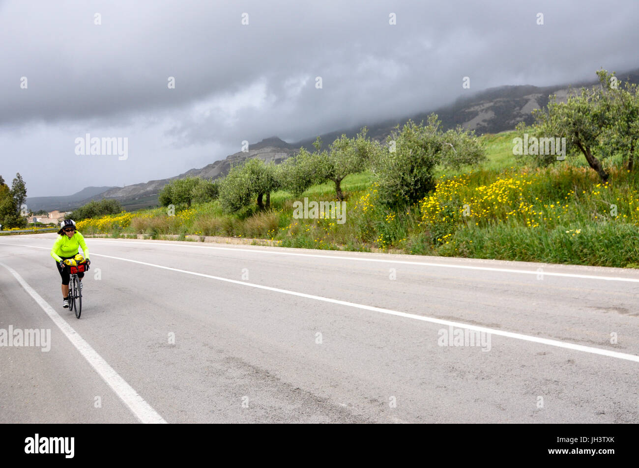 A female touring cyclist on a country road and storm clouds looming ...