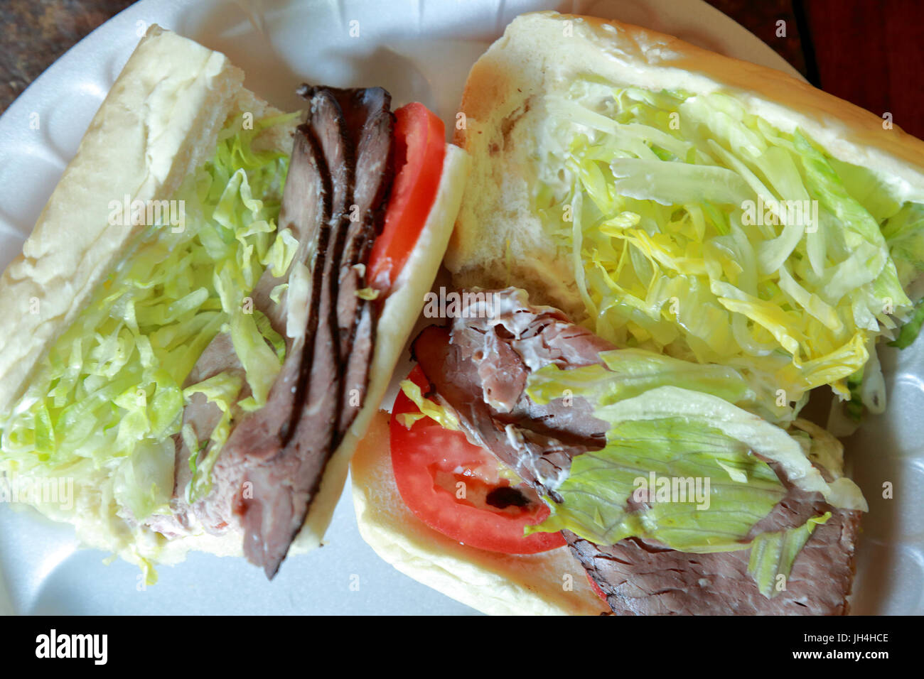 Roast beef submarine sandwich cut in two with bun open to show meat ...