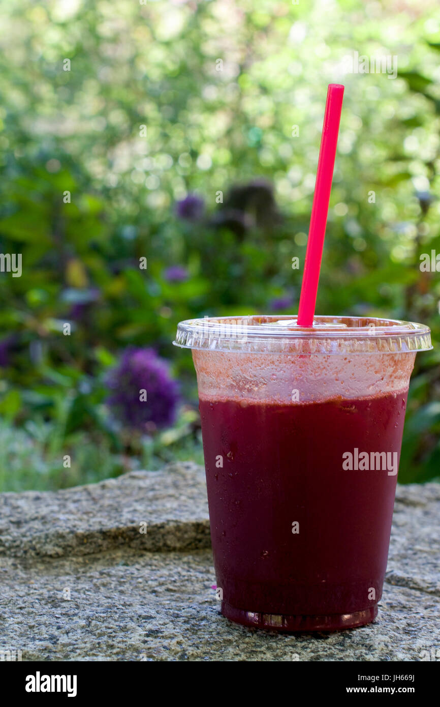 A carry-out plastic cup with a straw filled with beet juice outdoors on ...