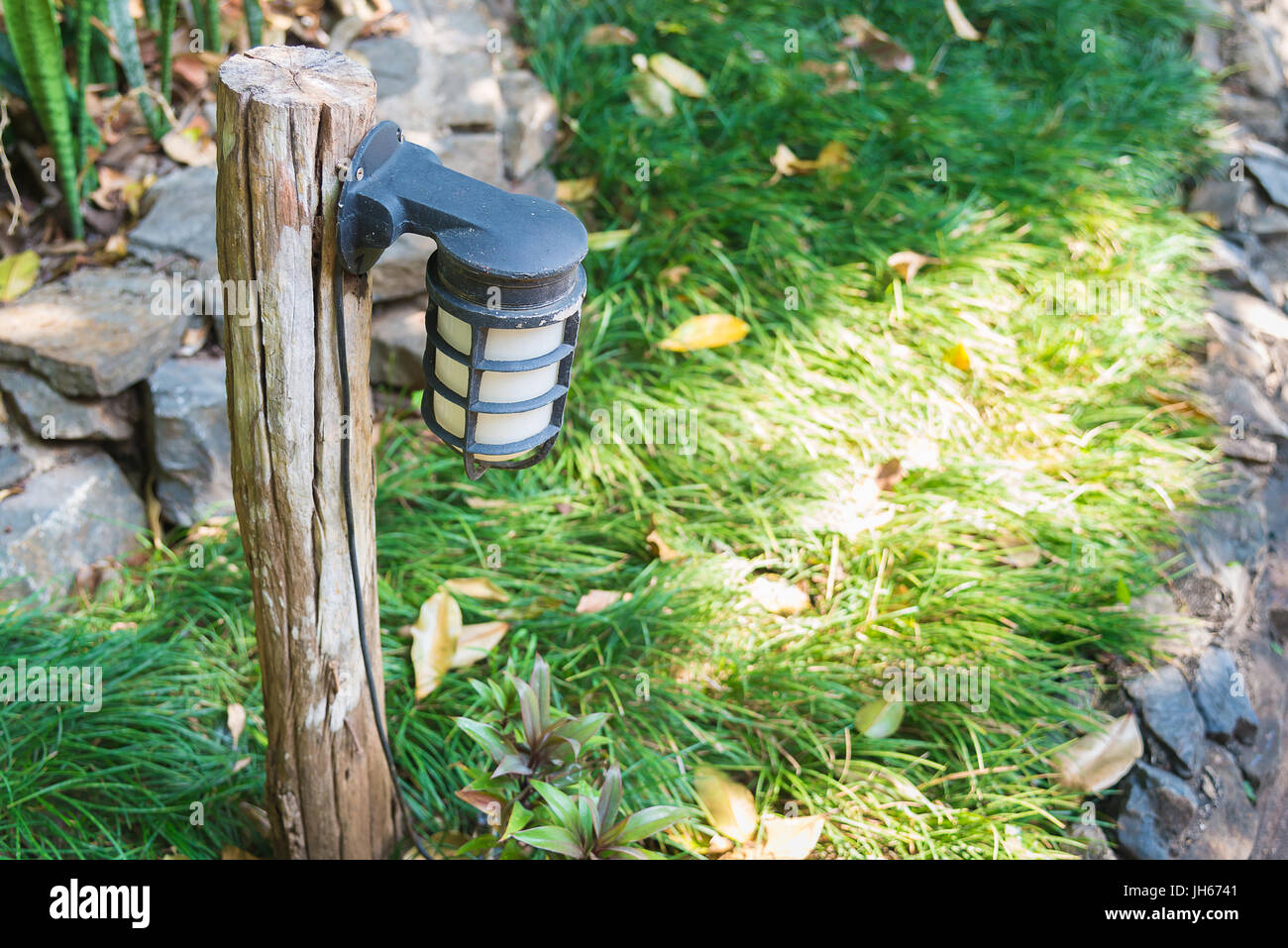 Old lamp on a short wooden pole with grass and tree in tropical garden ...