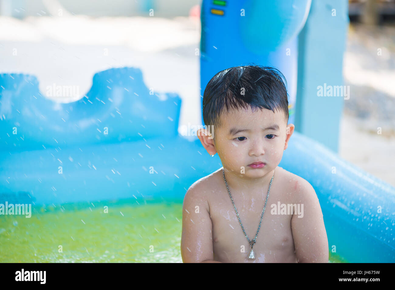 Sad Asian kid playing alone in inflatable baby pool. Boy swim and ...