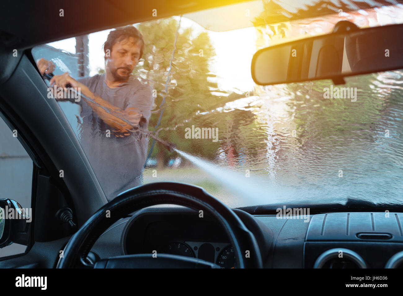 Man washing car in self-service car wash station, viewed from inside of ...