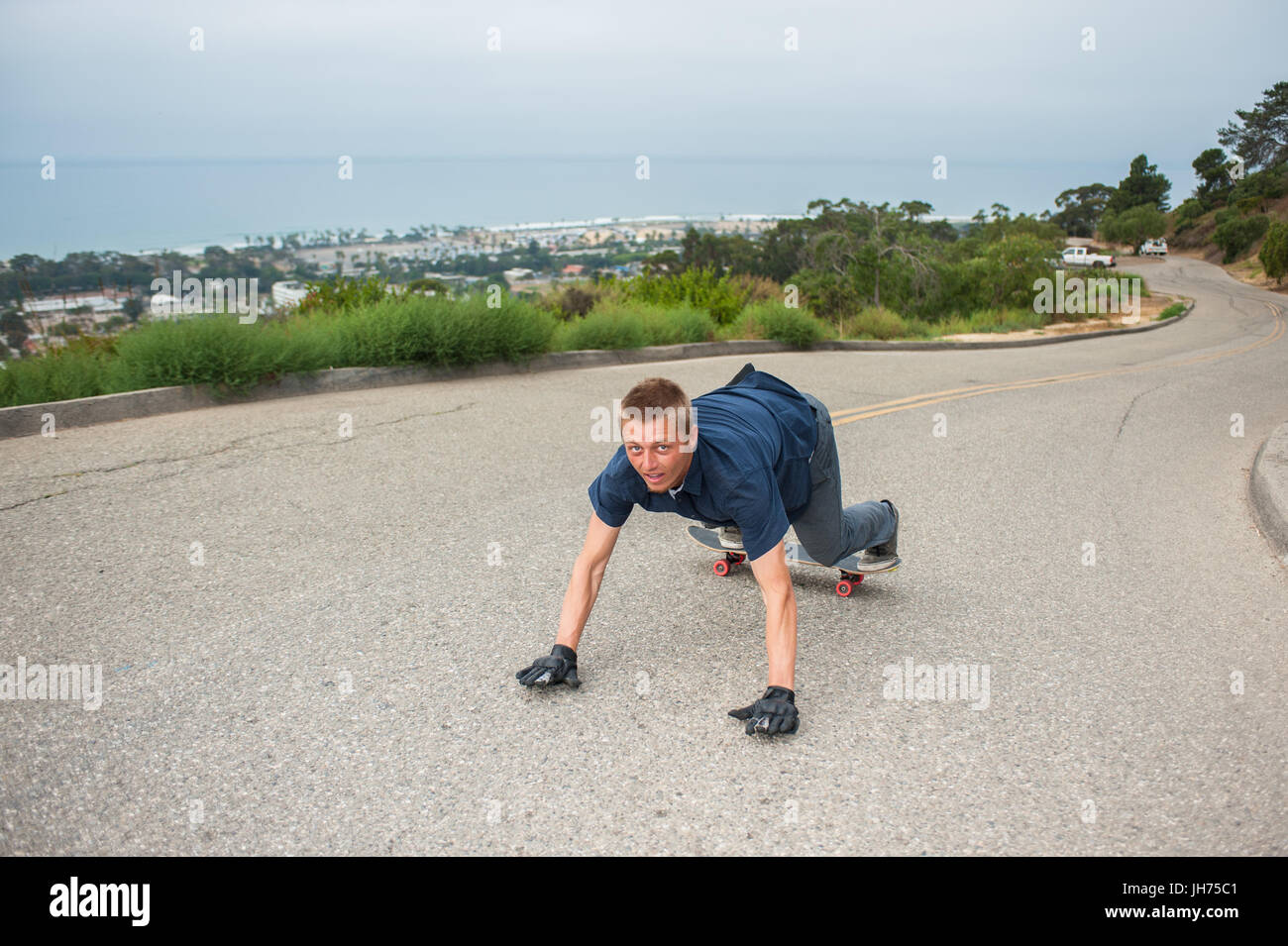 Downhill Skateboarder using gloved hands to skid around the corner from ...