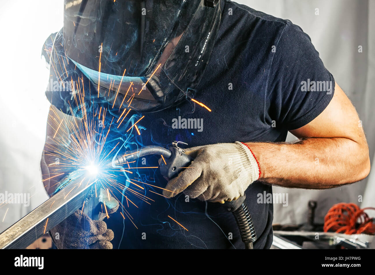 A strong man welder in a black T-shirt, in a welding mask and welders ...