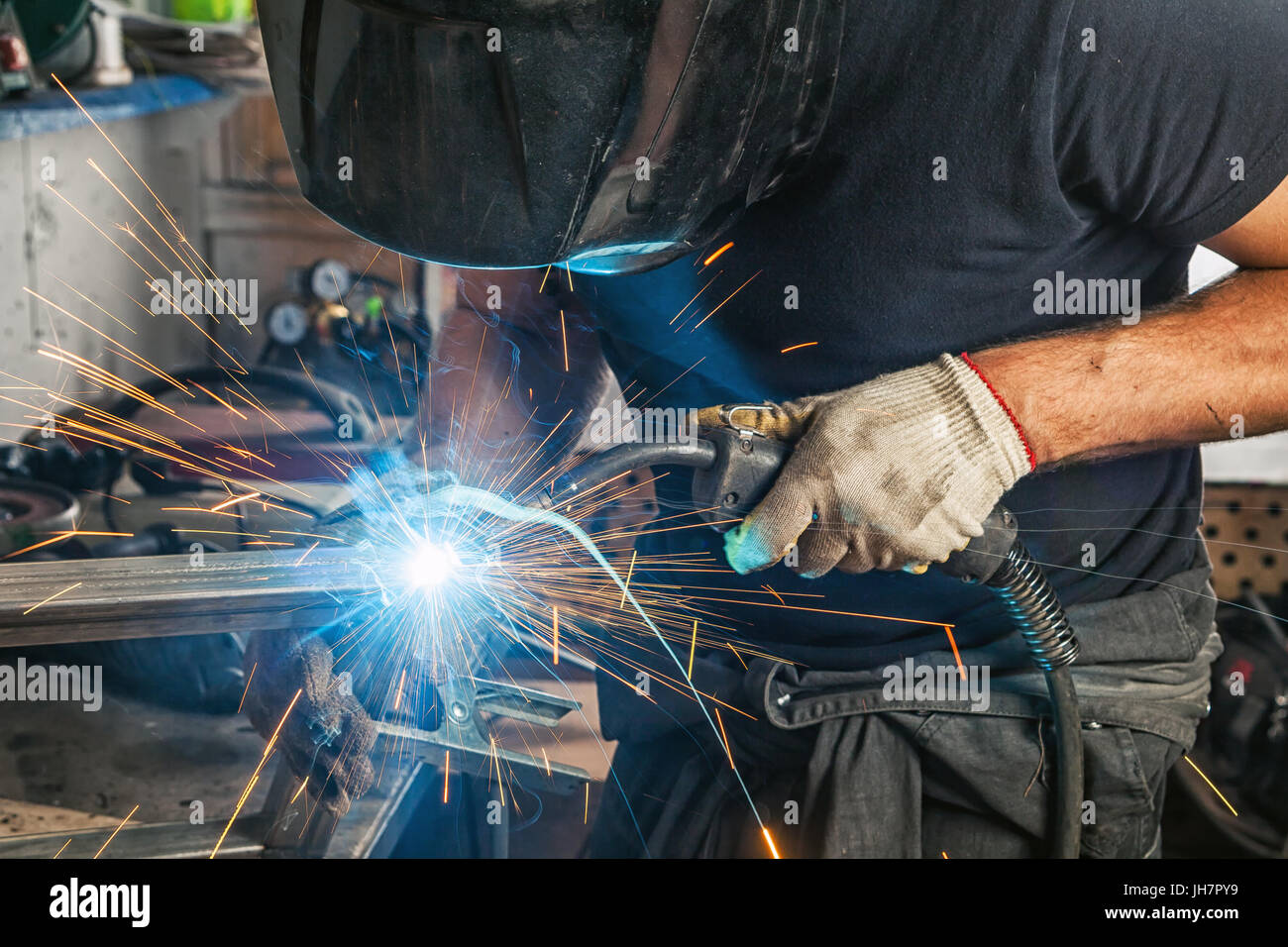 A strong man is a welder in a black T-shirt, in a welding mask and ...