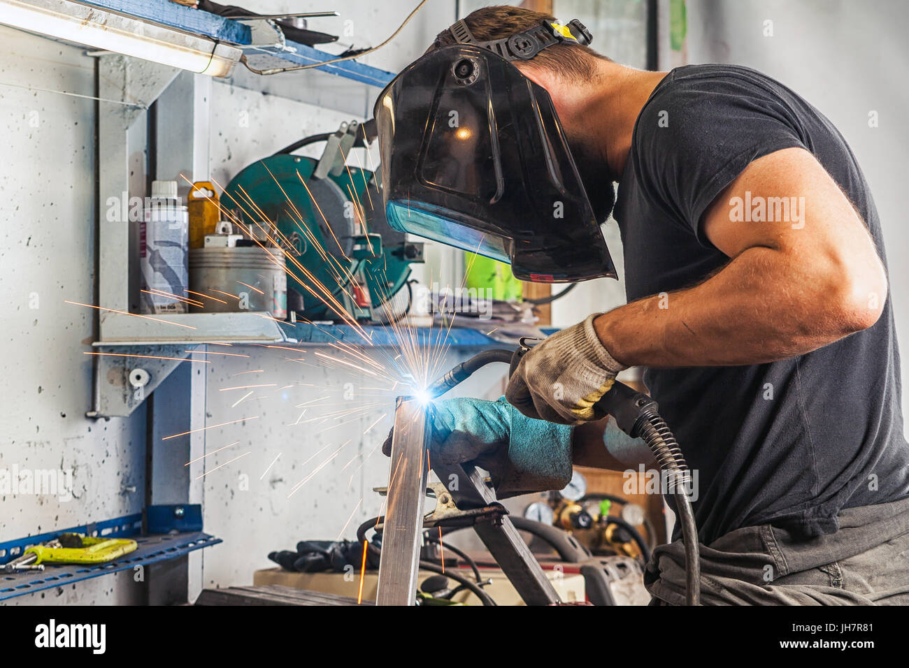 A young brunette man welder in a black T-shirt, in a welding mask and ...