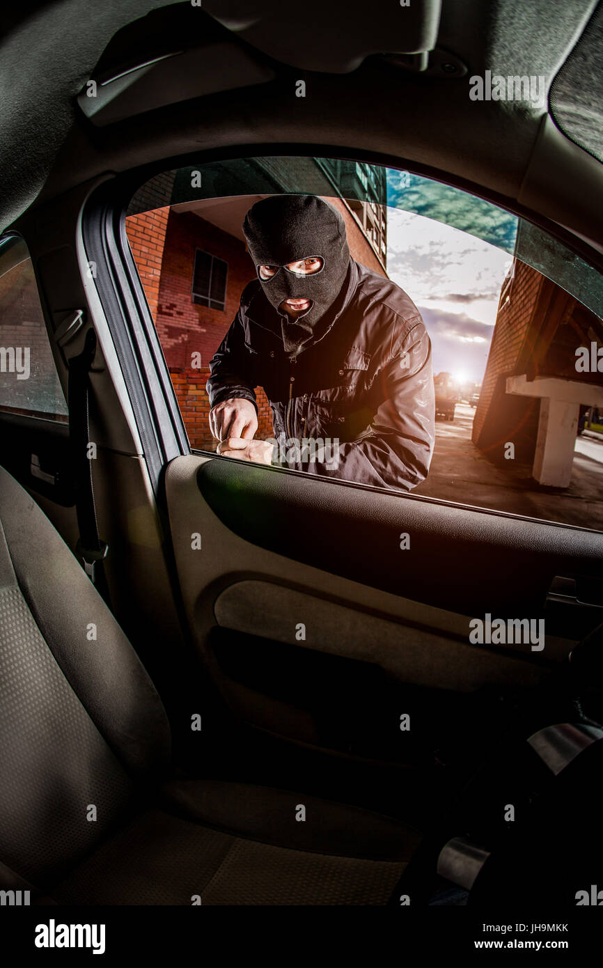 Robber and the car thief in a mask opens the door of the car and ...